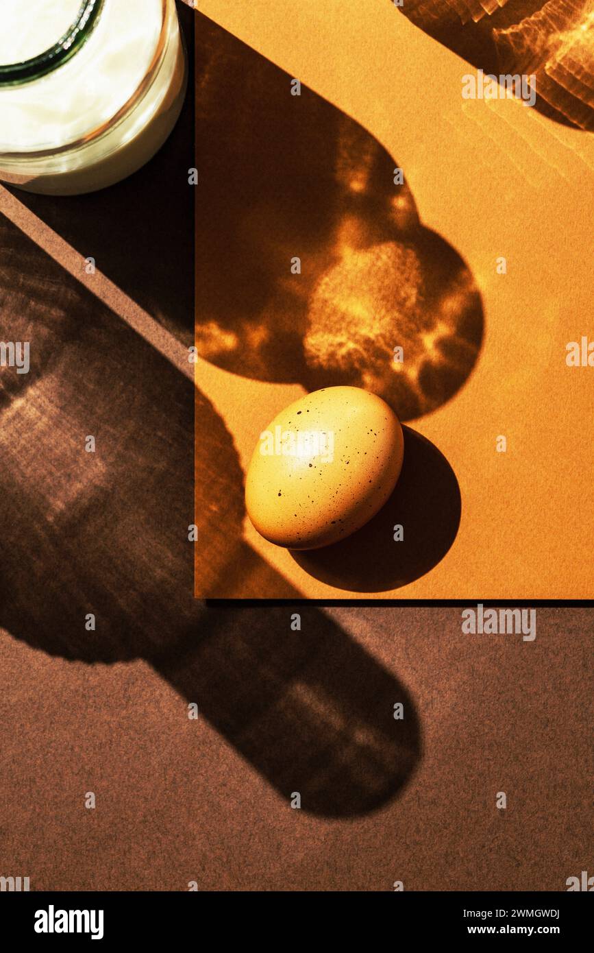 Egg and bottle of milk under direct light with long shadows on brown ...
