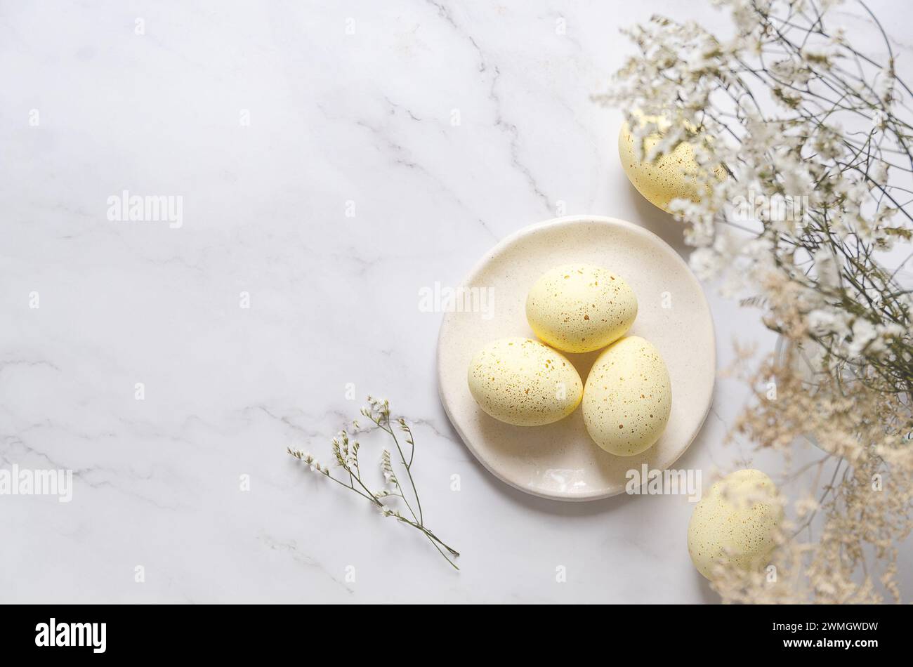 Yellow Easter eggs with golden spots on a plate and flowers on white ...