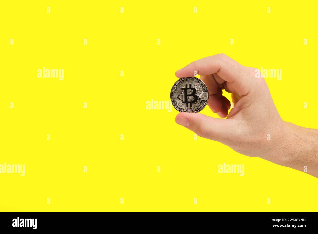 Bitcoin Coin Grasped in Hand on Yellow Backdrop. Symbolic of digital ...