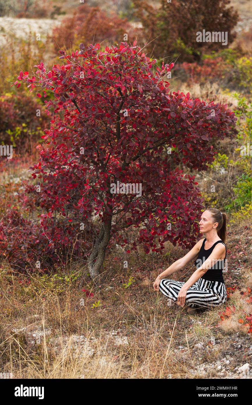 A young adult woman sits in the lotus position against a background of ...