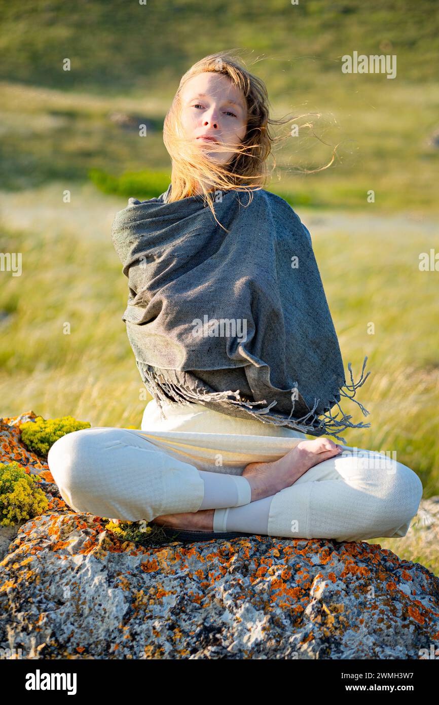 Young adult woman in yoga suit and stole sits in lotus position on a ...
