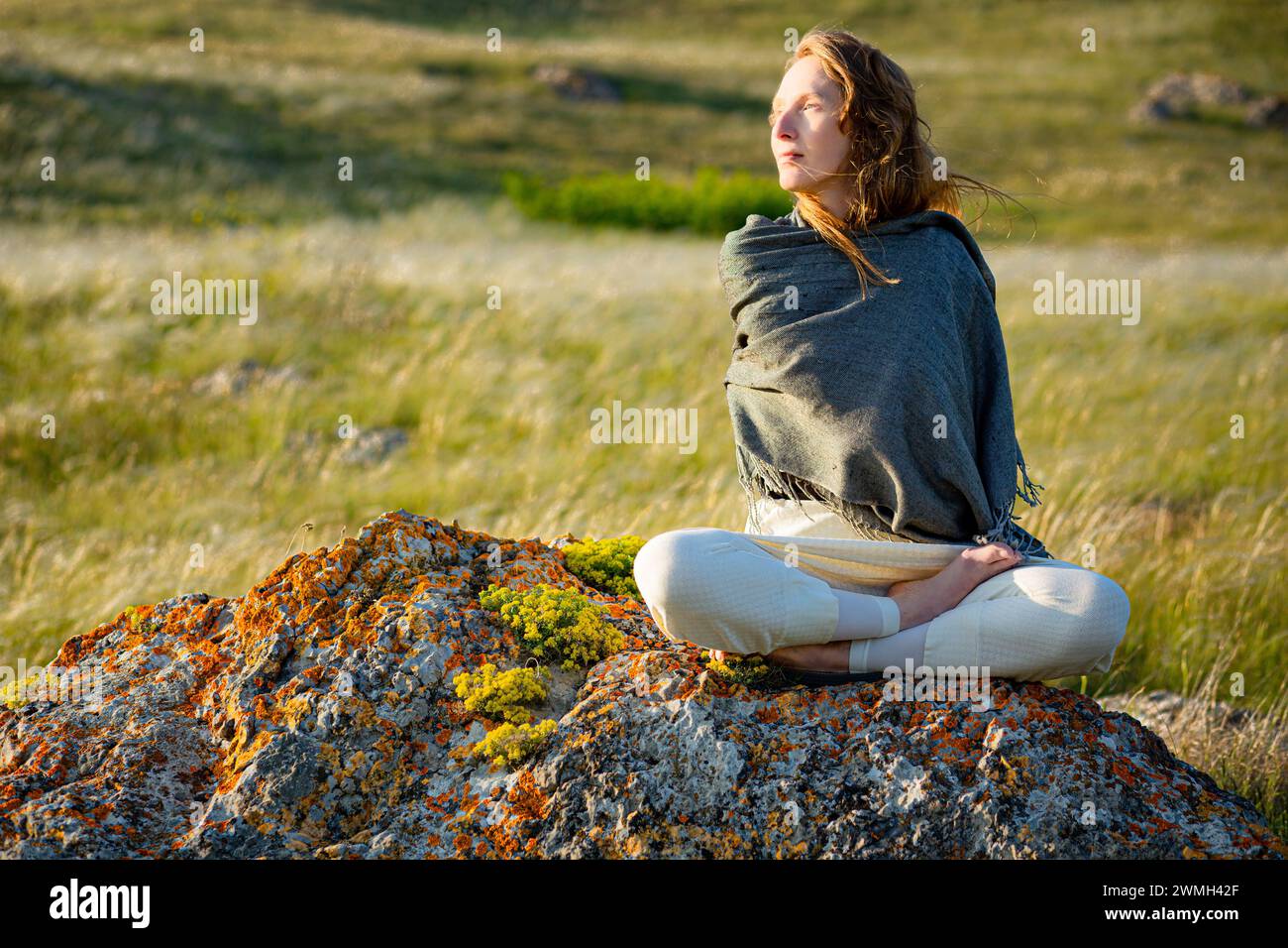 Young adult woman in yoga suit and stole sits in lotus position on a ...