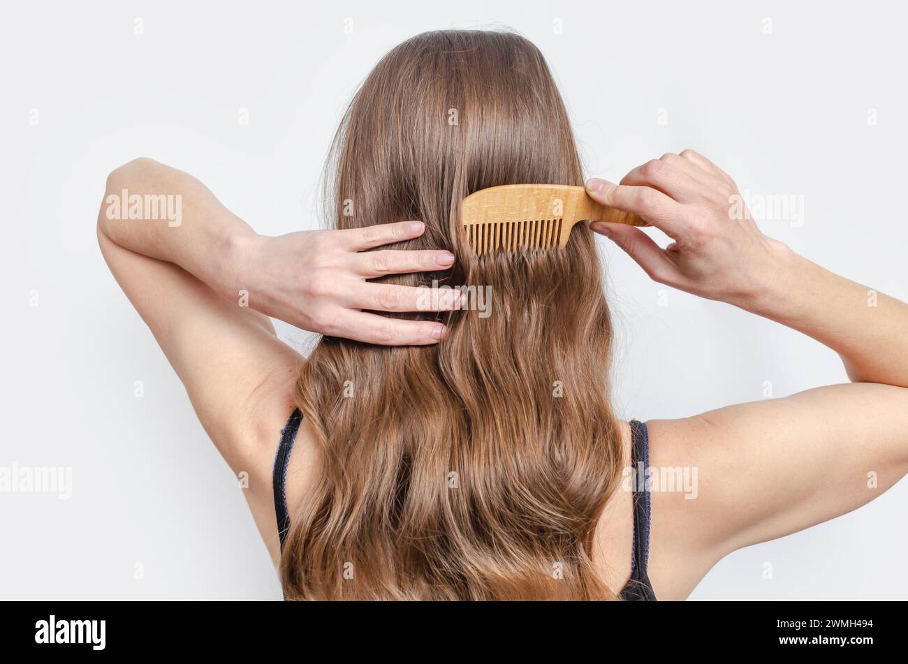 Woman combs her wavy hair with wooden comb on gray background. Takes ...