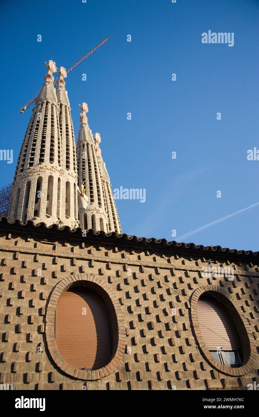 A tall structure behind a brick building: Sagrada Familia in Barcelona ...