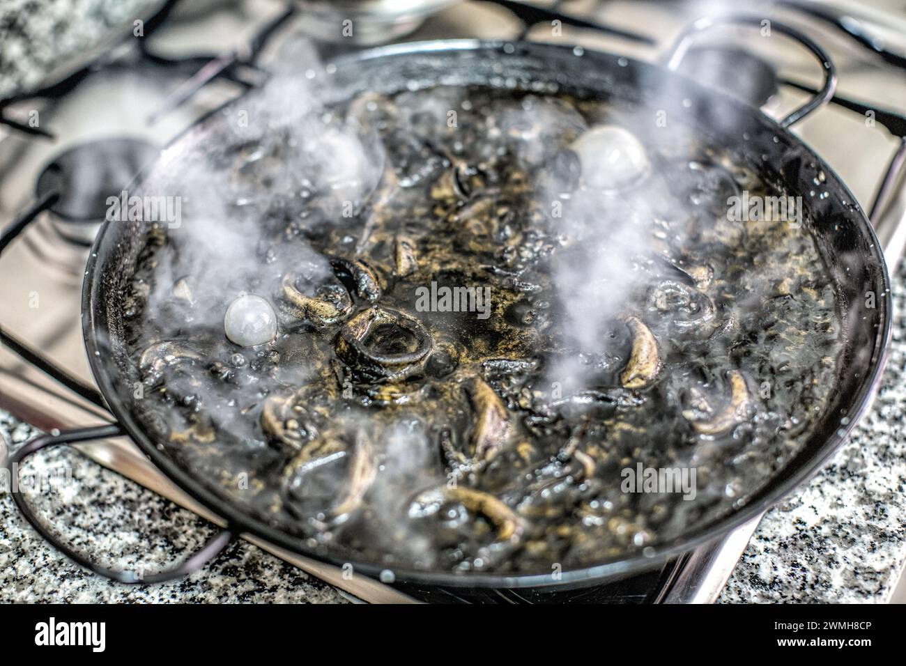 A simmering pan of black rice paella on a gas stove Stock Photo - Alamy