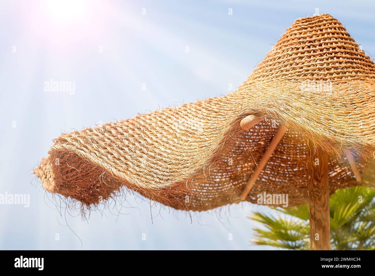 Wicker sun umbrella looks like a hat against blue sky and sun rays ...