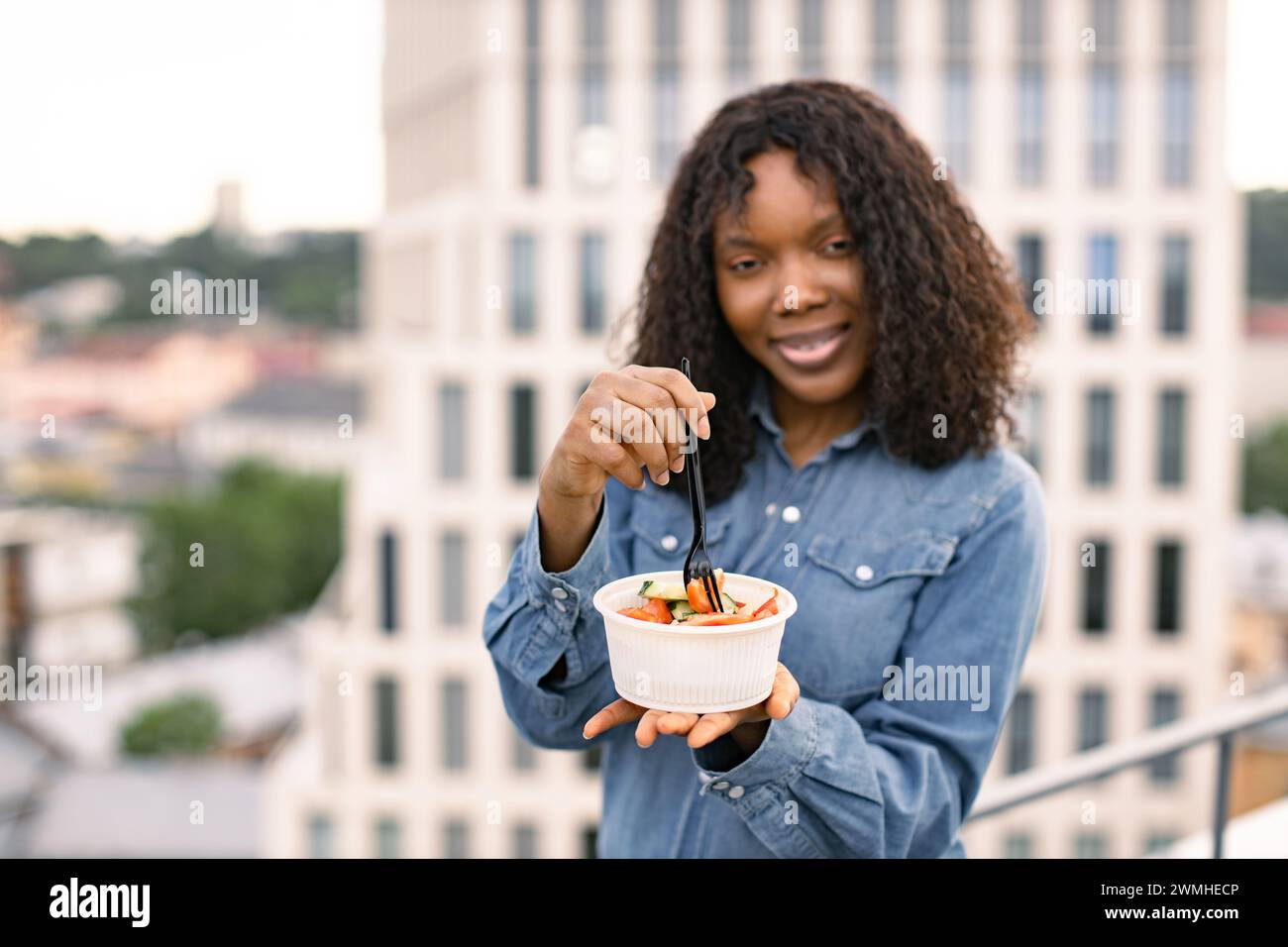 African businesswoman eating healthy salad standing on rooftop on a ...