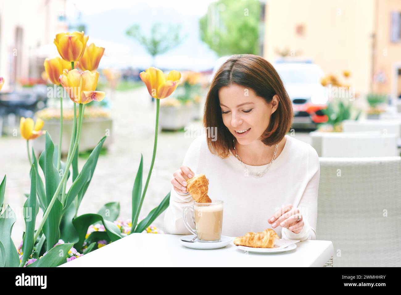 Portrait of happy mature woman having coffee with croissant in outdoor ...