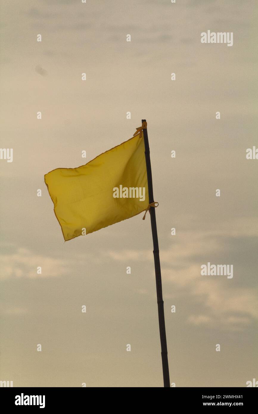 One centered yellow flag waving with the wind with a cloudy sky ...