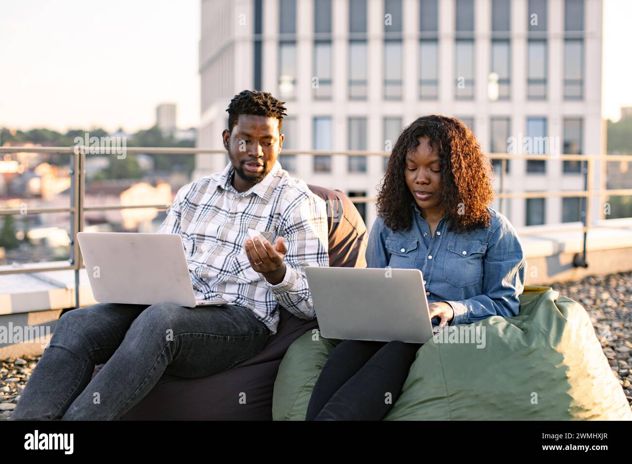 Two African business people discuss project sitting with laptops on ...
