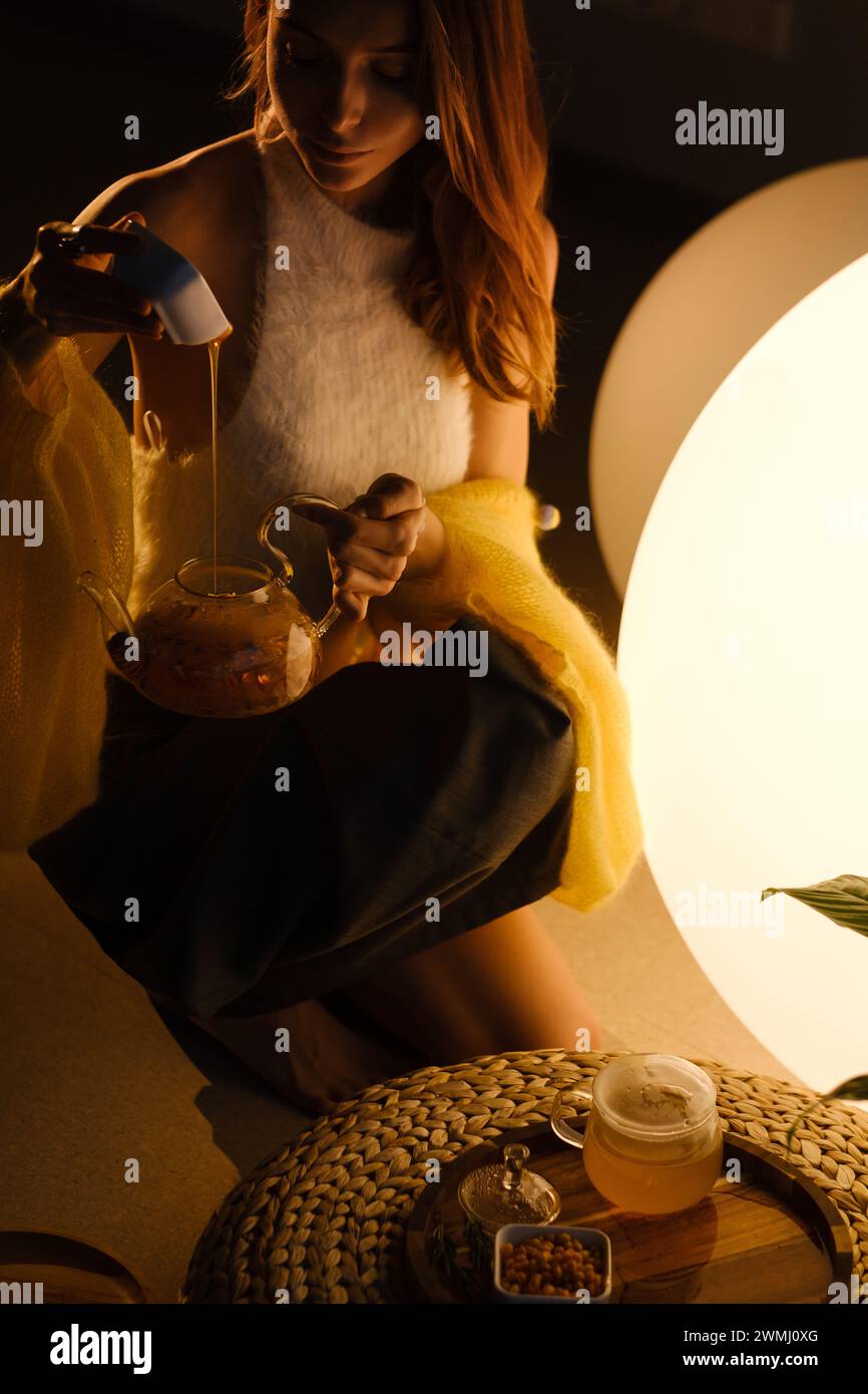 A young girl conducts an evening tea drinking procedure indoors ...