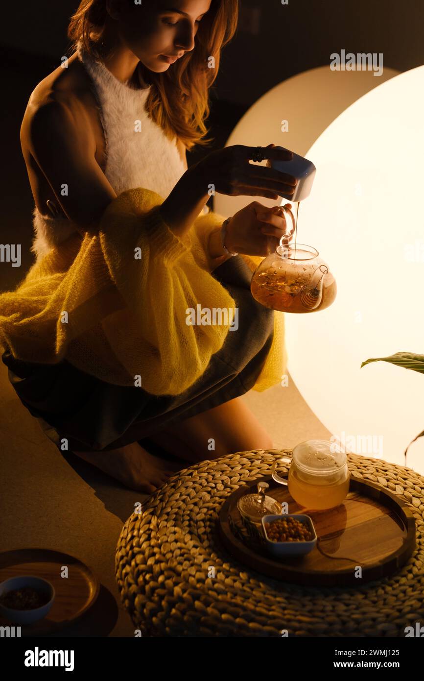 A young girl conducts an evening tea drinking procedure indoors ...