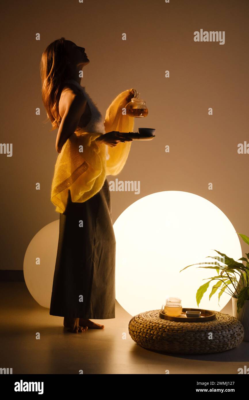 A young girl conducts an evening tea drinking procedure indoors ...
