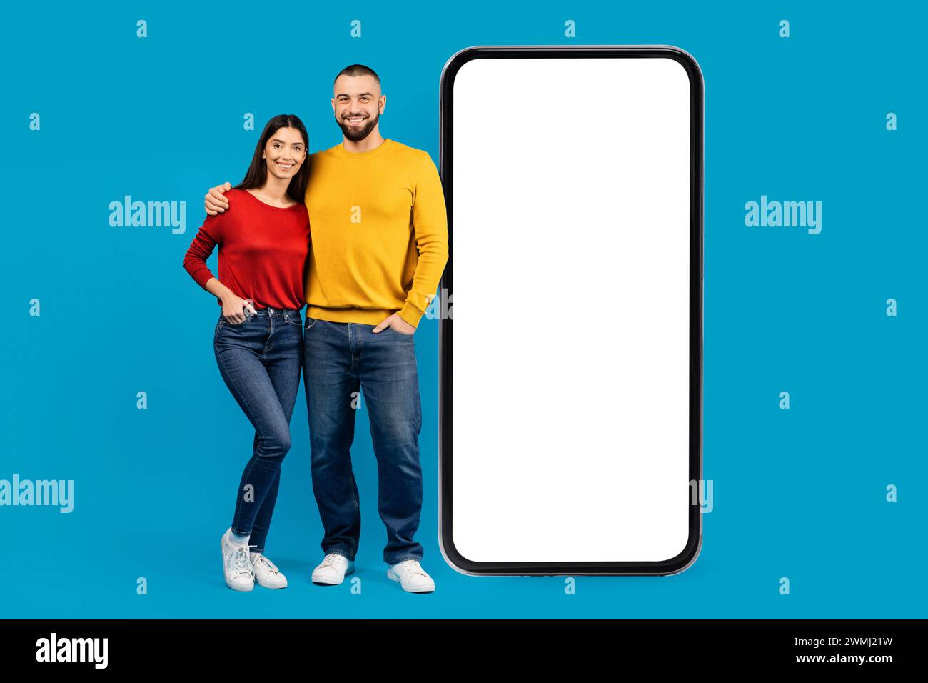 Happy young couple standing next to giant smartphone with blank white ...