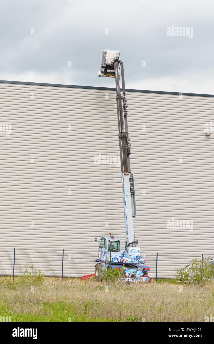 A worker lifts materials onto the roof of a gray warehouse with a ...