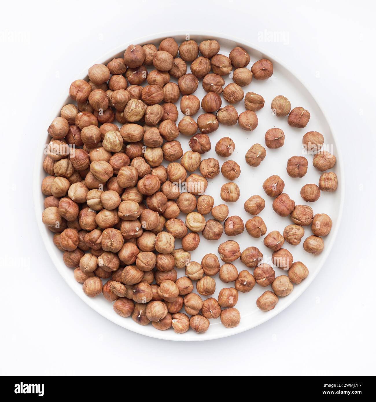 A bounty of hazelnuts fills a white plate, their warm brown tones and ...