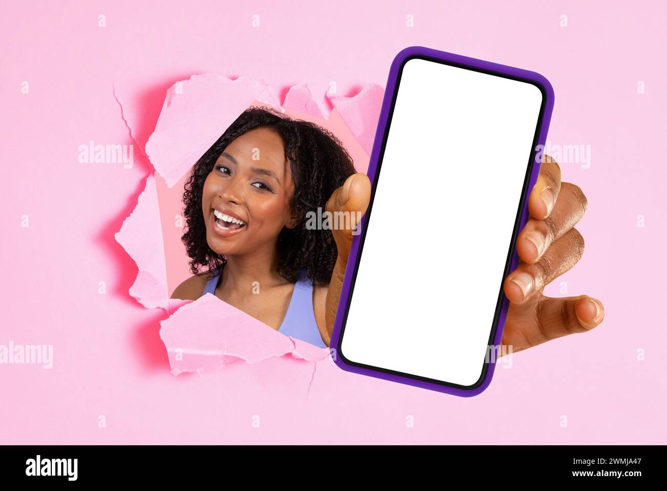 Cheerful woman peeking through a torn pink paper wall presenting a ...