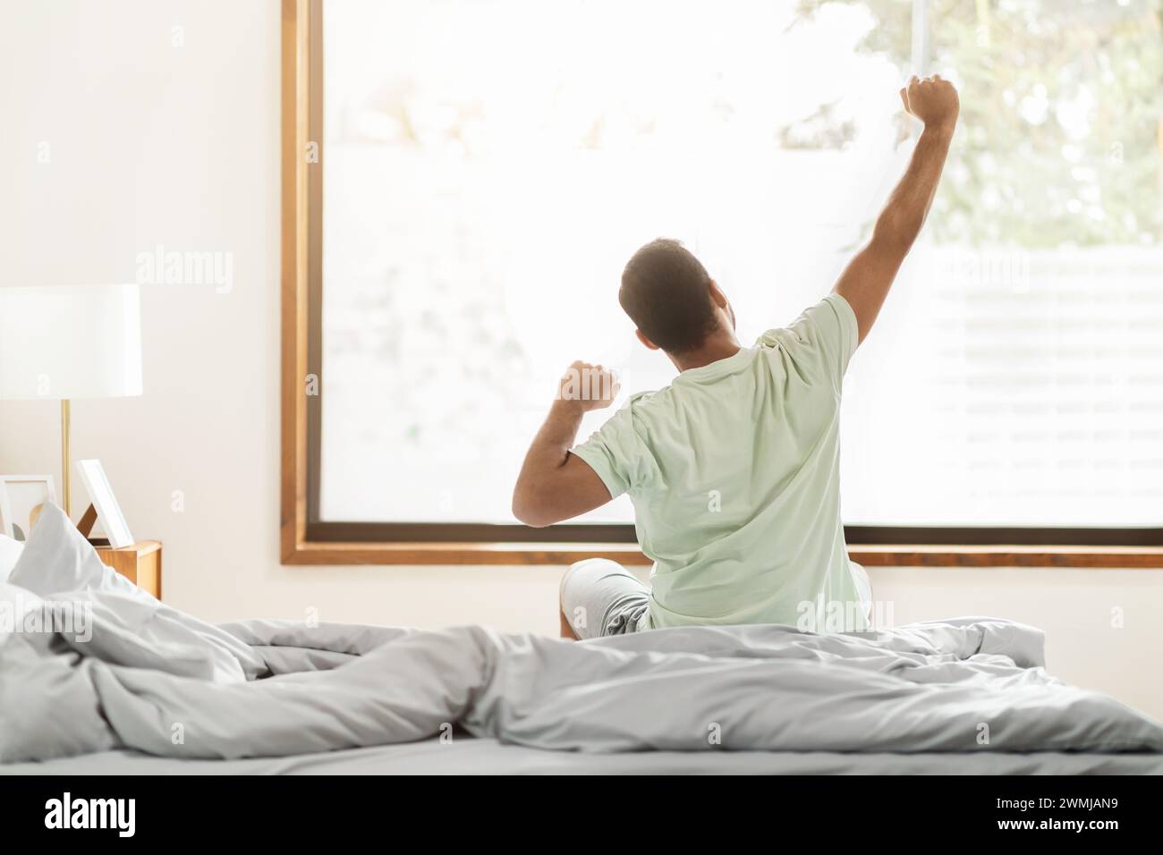 Back view of fully-rested man sitting on bed, stretching body Stock ...