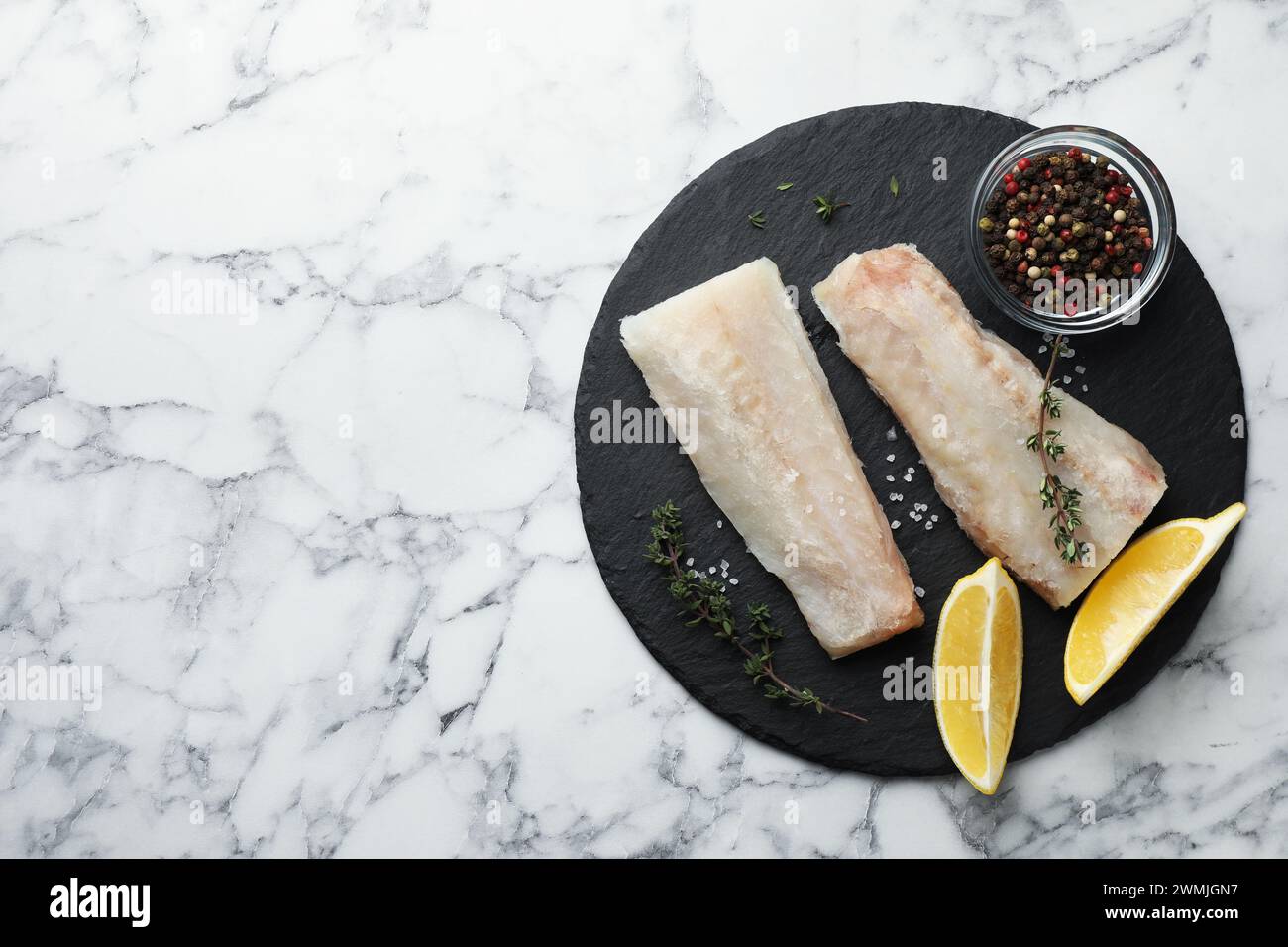 Fresh raw cod fillets, spices and lemon on white marble table, top view ...