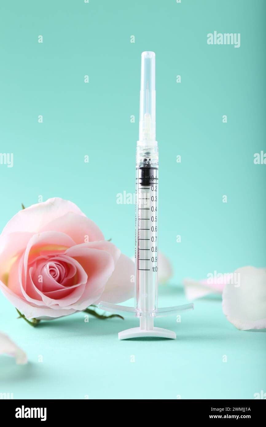 Cosmetology. Medical syringe, rose flower and petals on turquoise ...