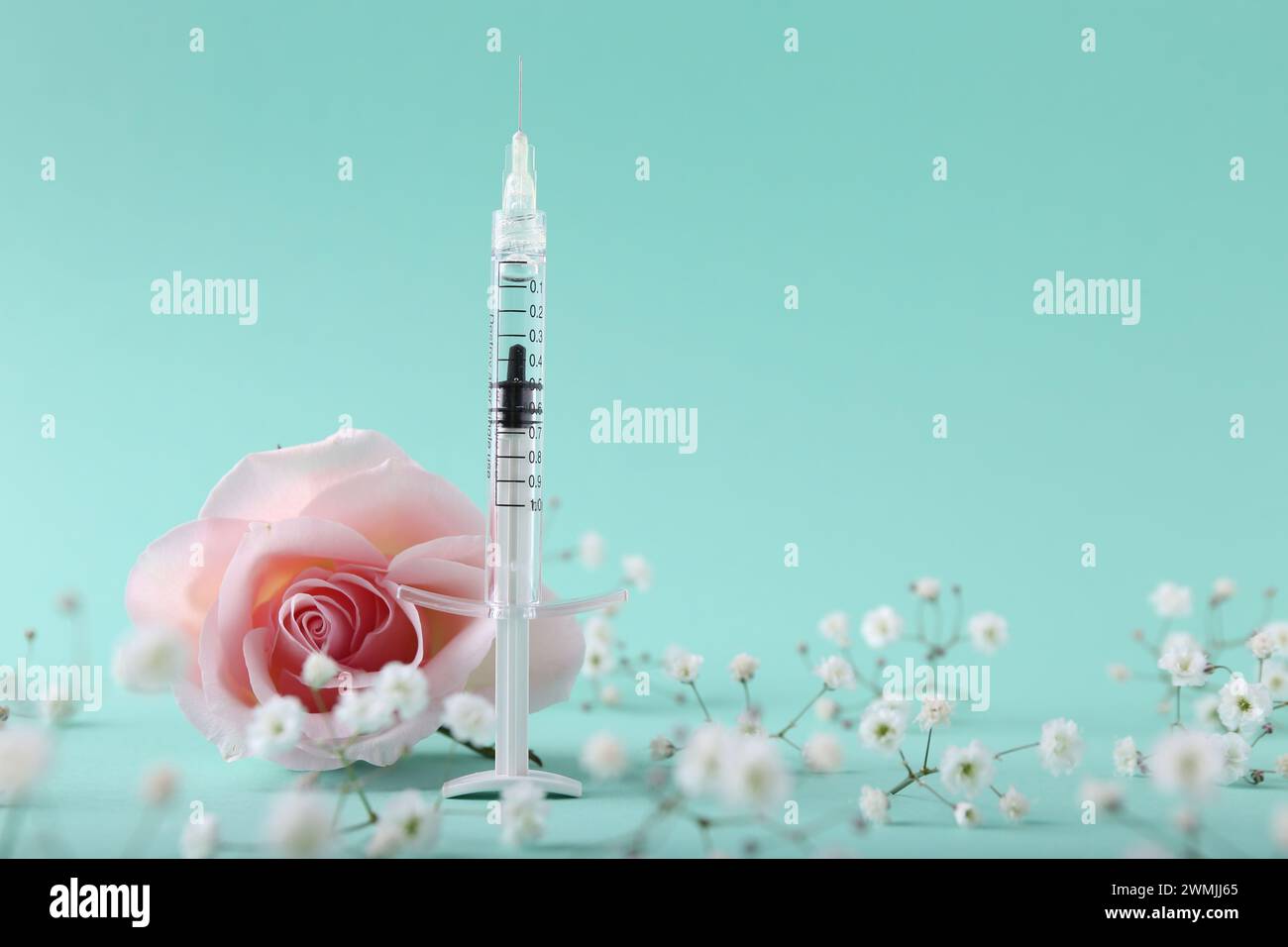 Cosmetology. Medical syringe, rose and gypsophila flowers on turquoise ...