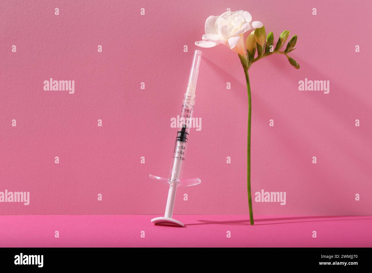 Cosmetology. Medical syringe and freesia flower on pink background ...