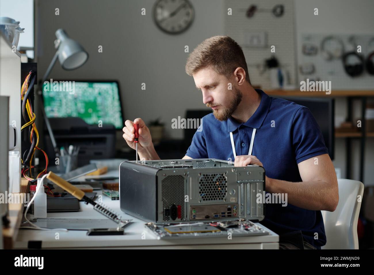 Young serious male technician in dark blue uniform sitting by workplace ...
