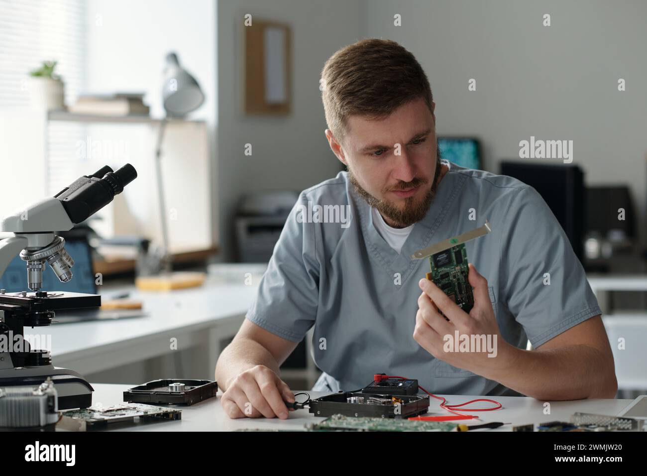 Young serious man in grey uniform looking at part of computer processor ...