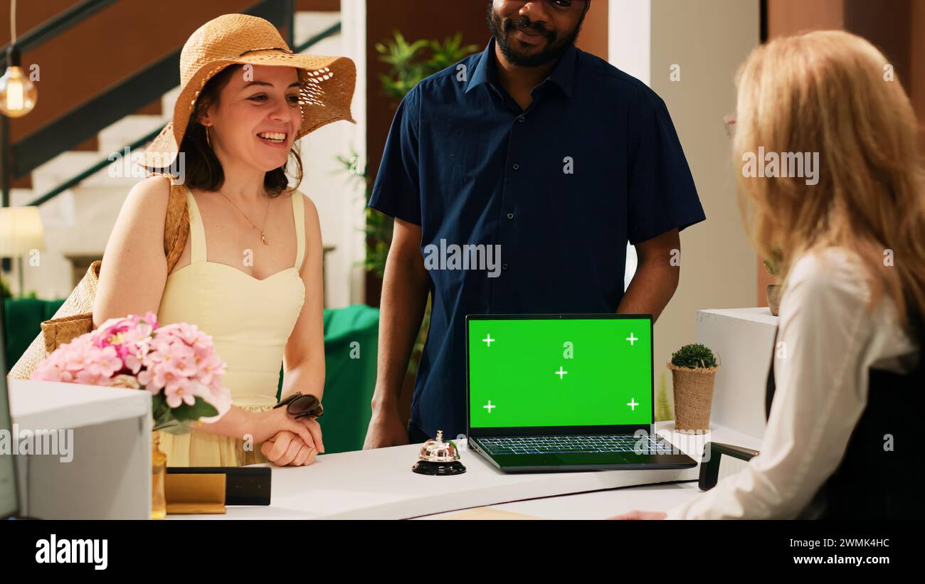 Receptionist welcoming tourists and using greenscreen display on laptop ...