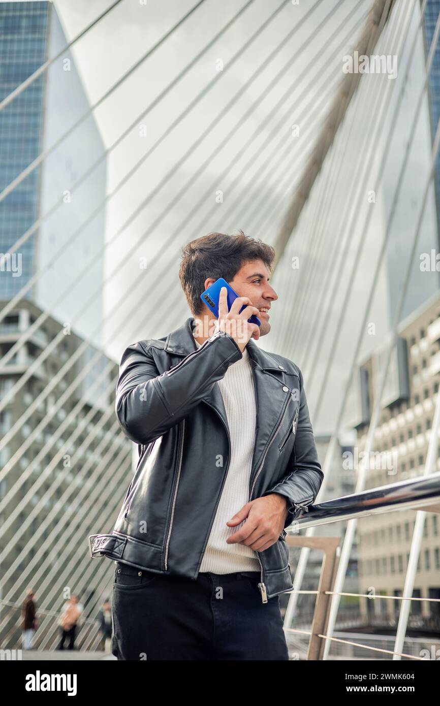 vertical dark-haired man talking on the phone leaning on railing with ...