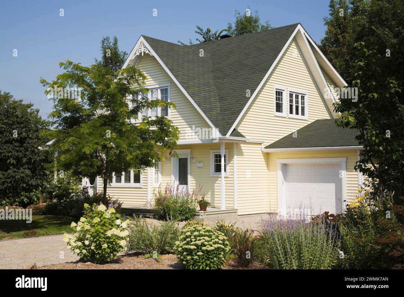 Two storied yellow clapboard with white trim home and landscaped front ...