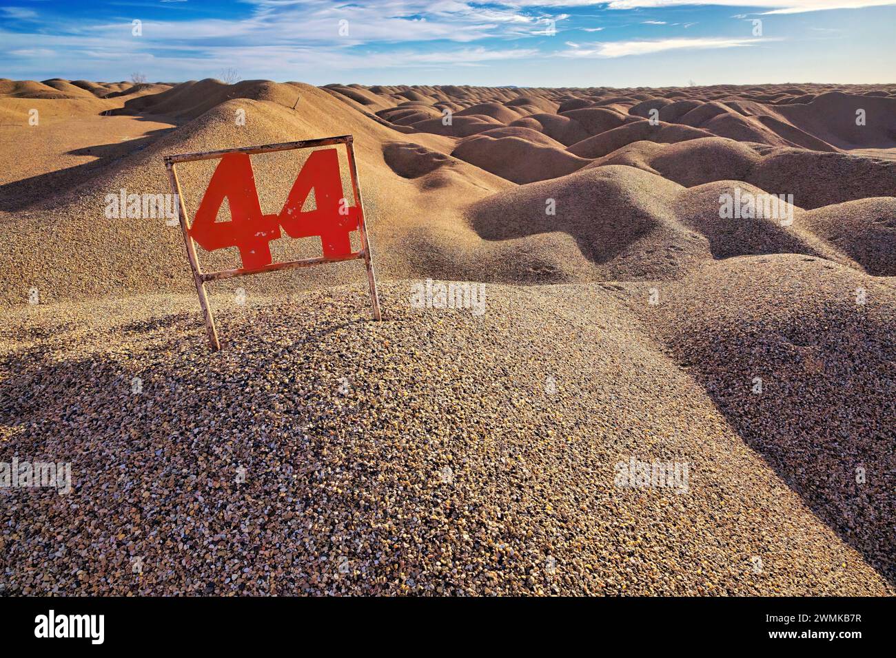 Sign '44' in red numbers is posted in a pile of gravel. Sediment that ...