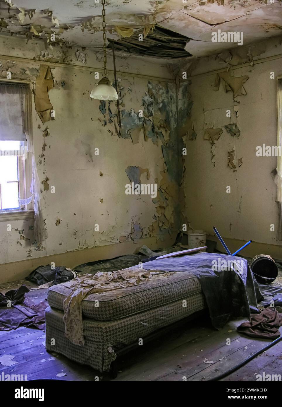 Abandoned bed in a decrepit room with damaged ceiling and walls and ...