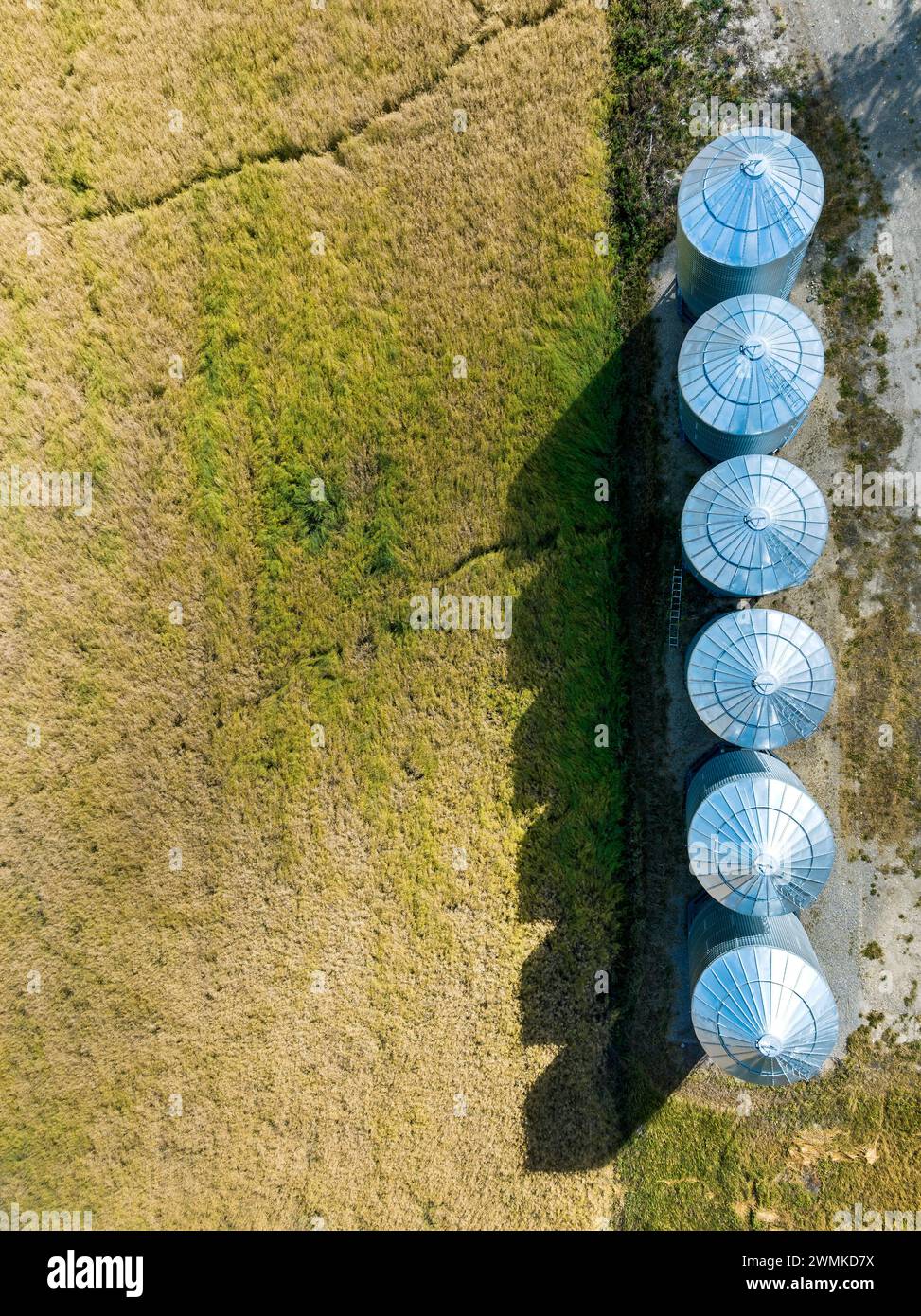 Aerial view of large metal grain bins in a row in a field, near ...