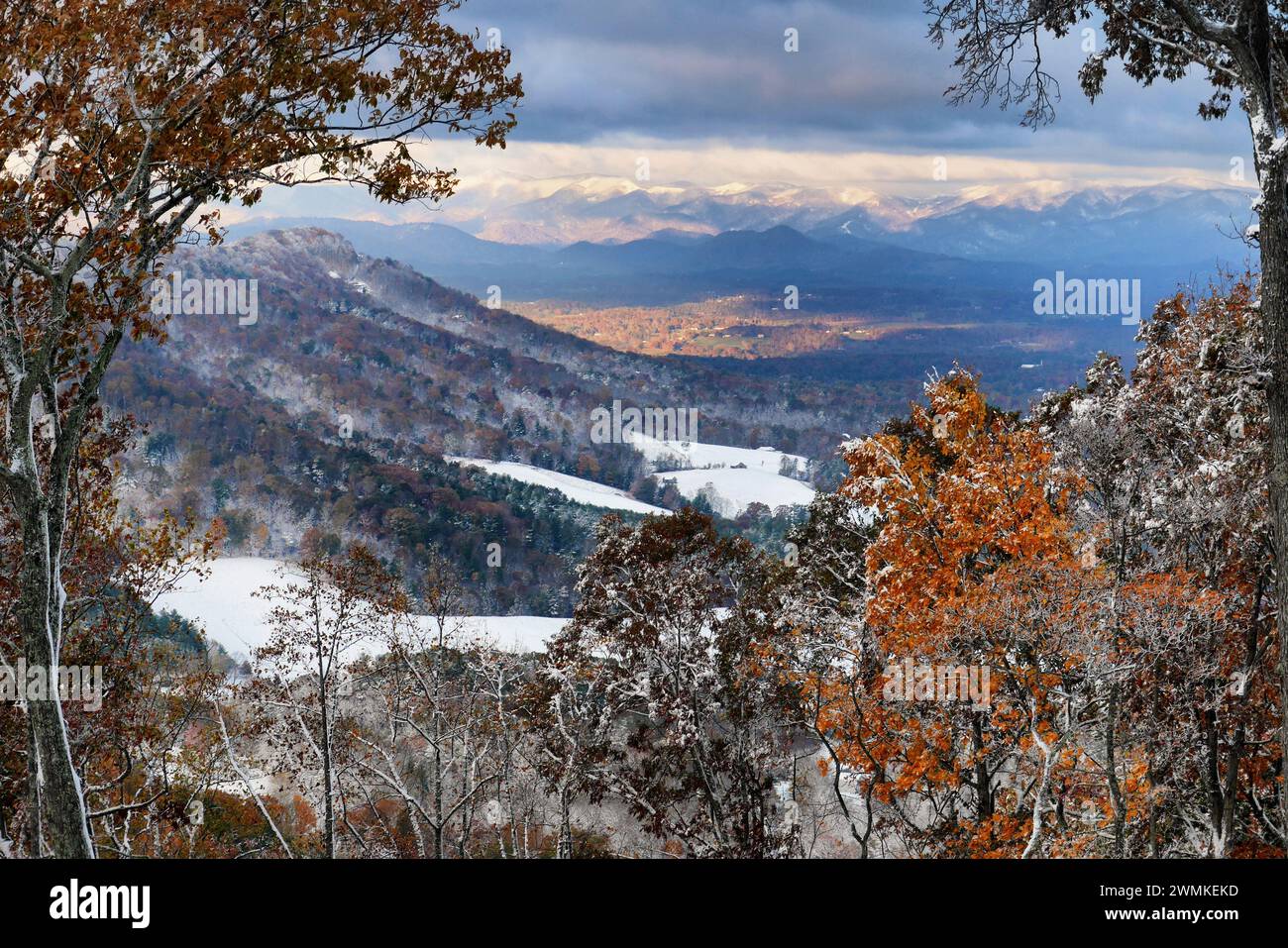 Snow-covered farming valley is framed by mountains and trees in autumn ...