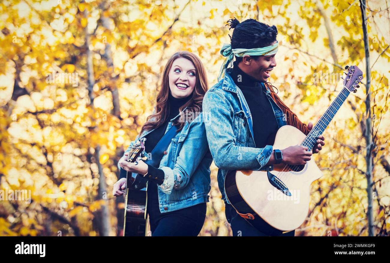 Mixed race married couple standing back to back, playing guitars during ...