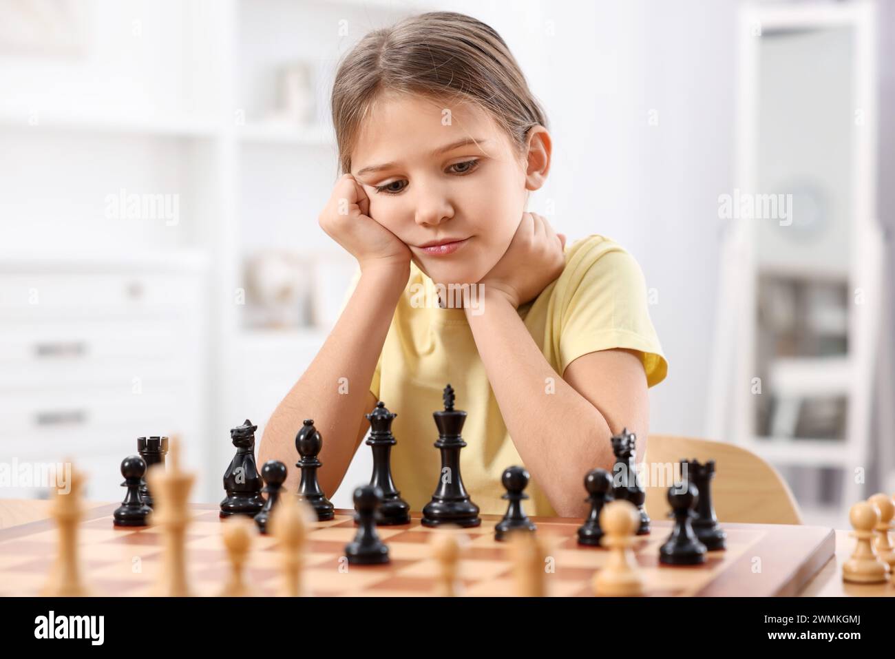 Cute girl playing chess at table in room Stock Photo - Alamy