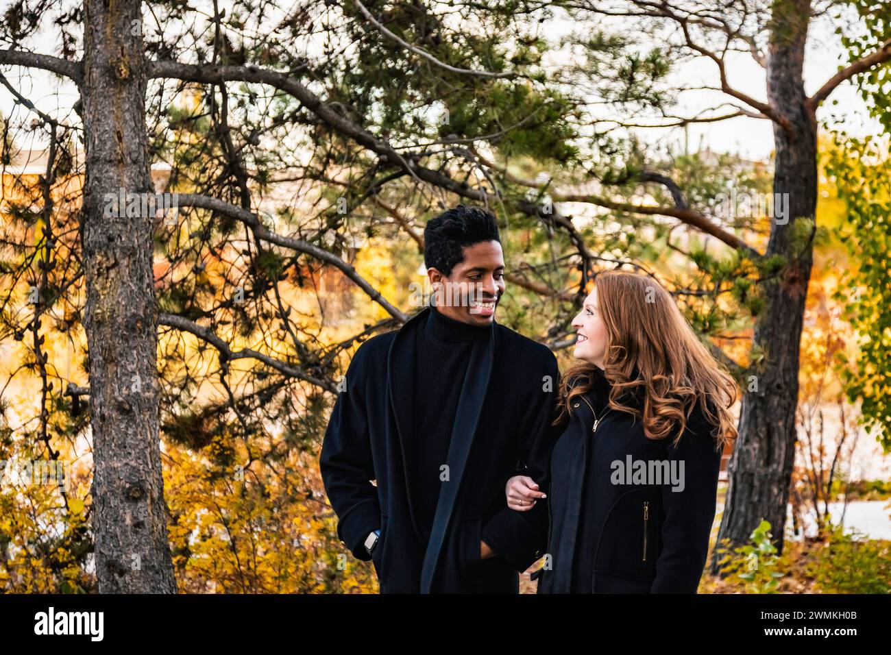 A mixed race couple smiling at each other walking through the woods ...