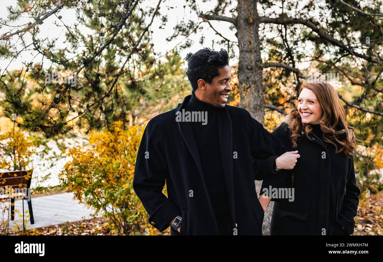 A mixed race couple smiling at each other walking through the woods ...