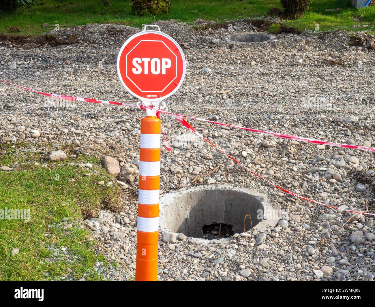 A stop sign in a park in front of an open manhole. Danger lies ahead. A ...
