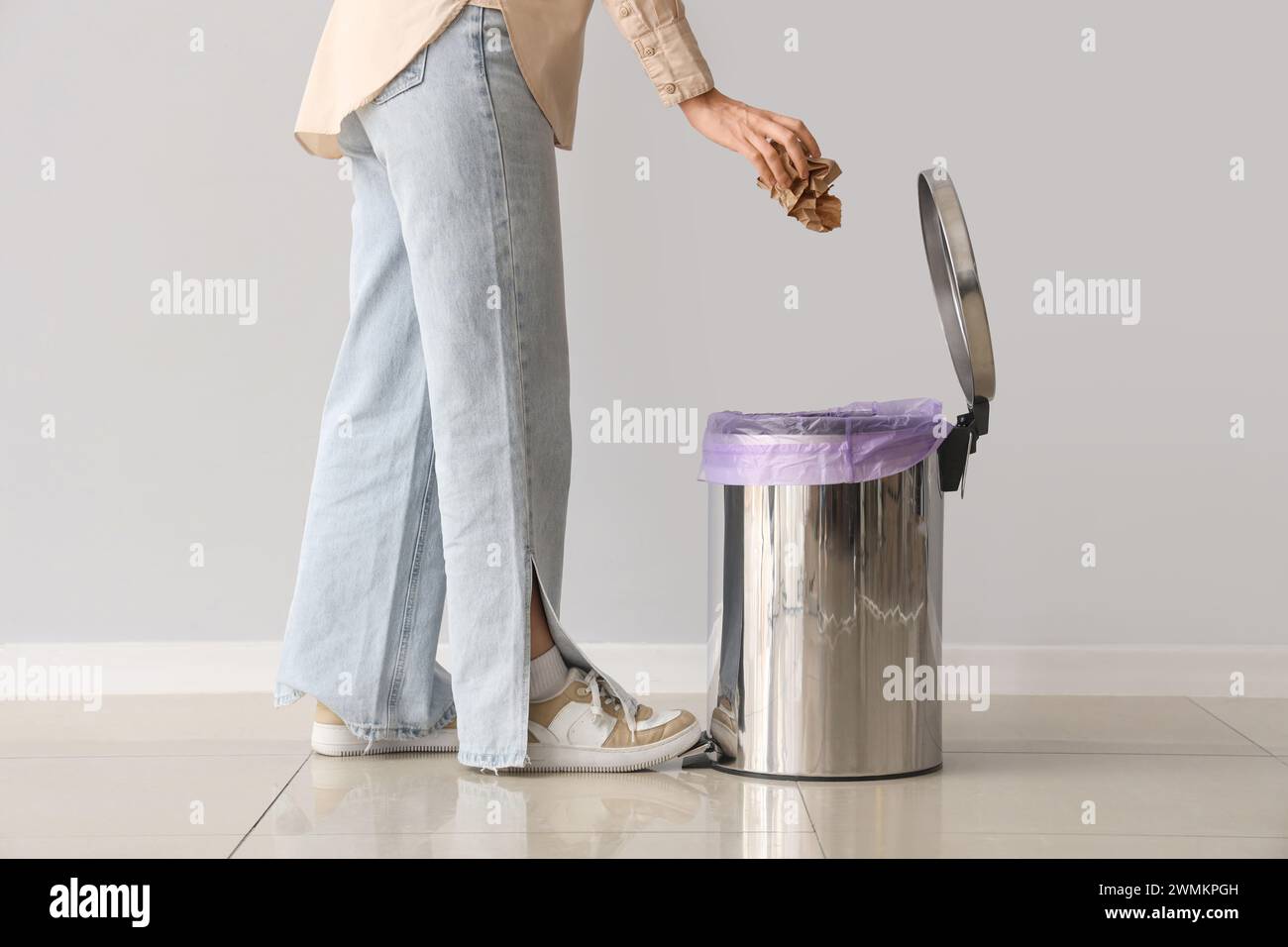 Woman throwing crumpled paper into trash bin with foot pedal near grey ...