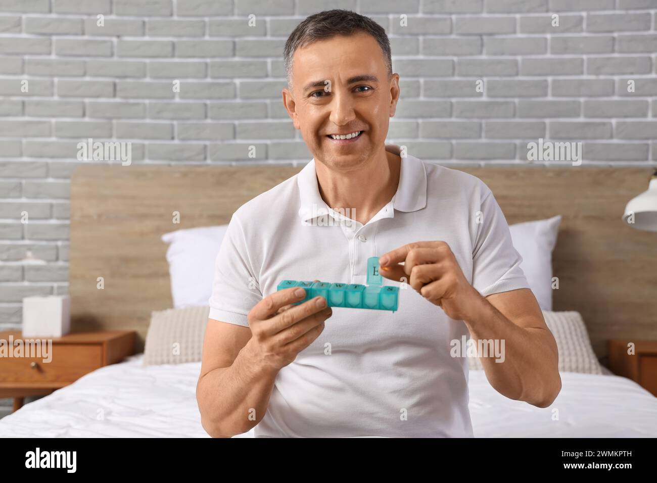 Middle-aged man taking pill from pillbox in bedroom Stock Photo - Alamy