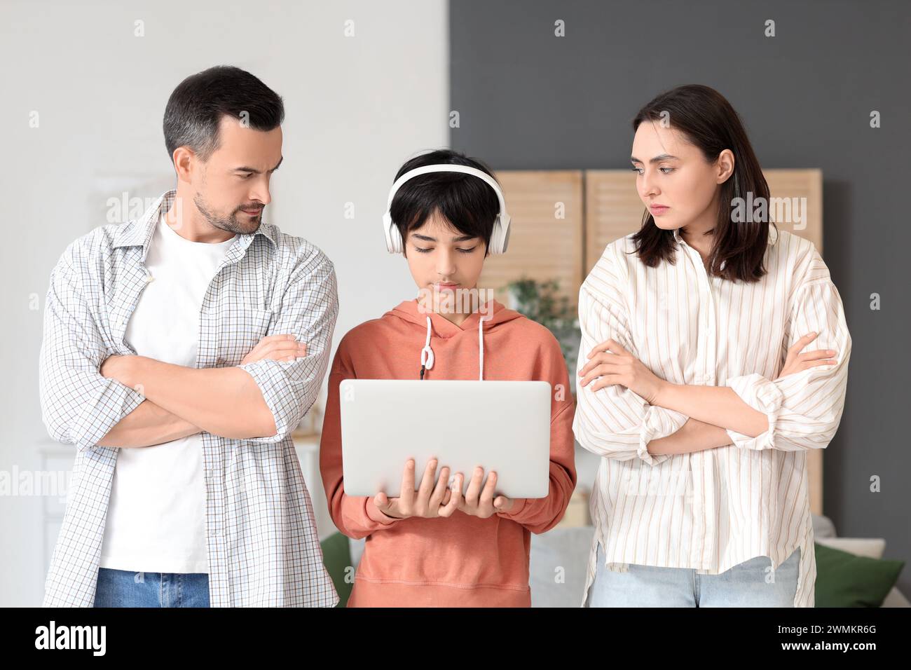 Teenage boy in headphones with laptop and his upset parents at home ...