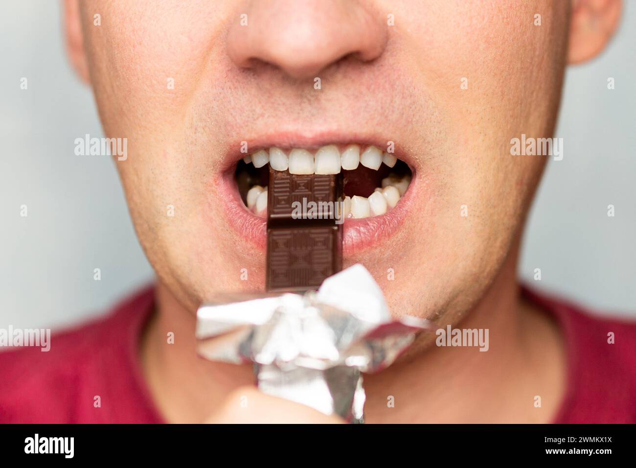 Mouth of man eating chocolate against blue background. A man's mouth in ...