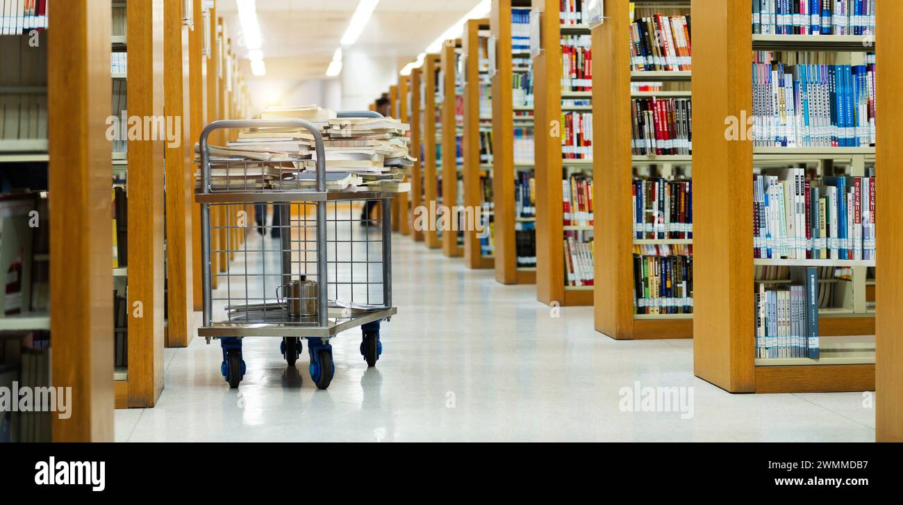 Interior of library with book shelves and books in cart Stock Photo - Alamy