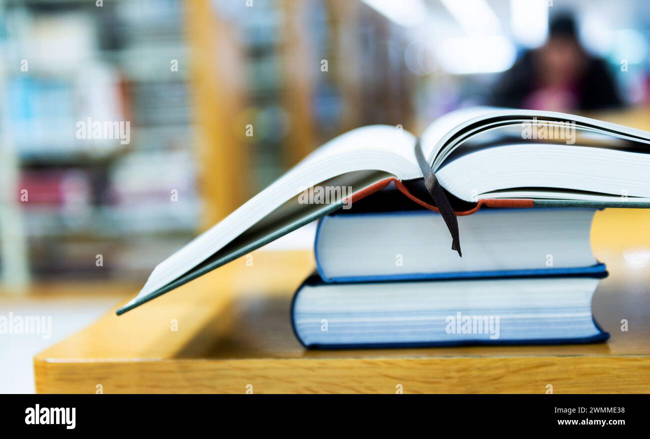 Stack of books opened on library desk Stock Photo - Alamy
