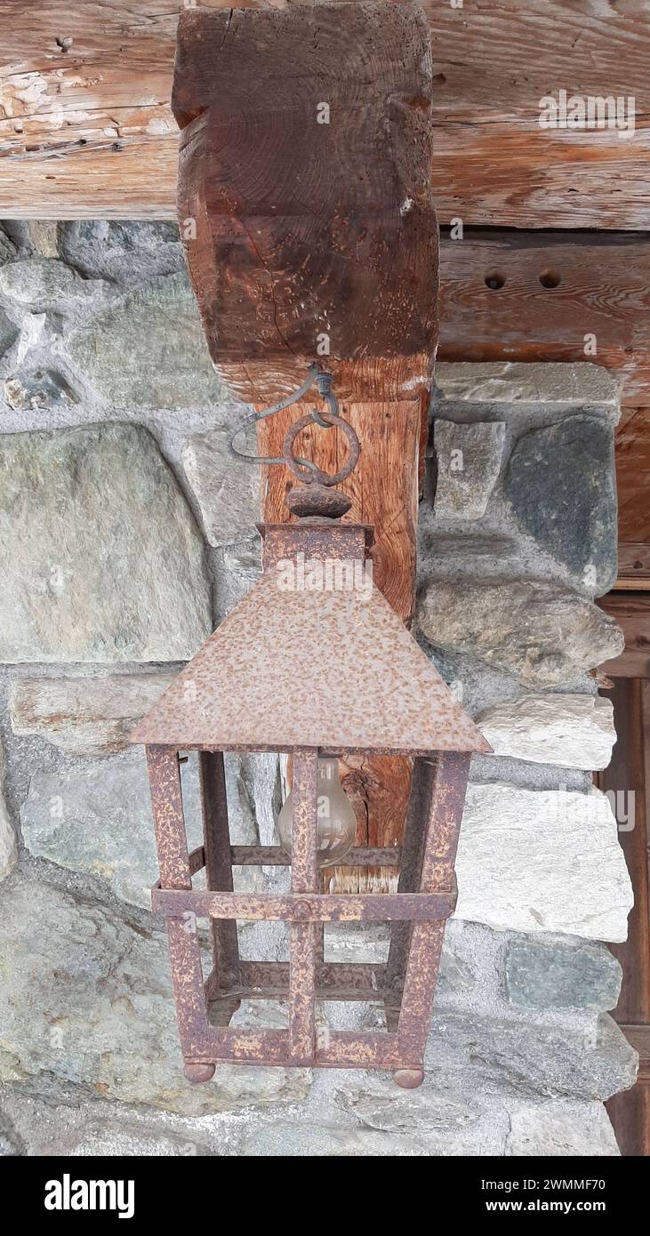 Old, rusted, iron lamp hanging from a wood and stone traditional cabin ...
