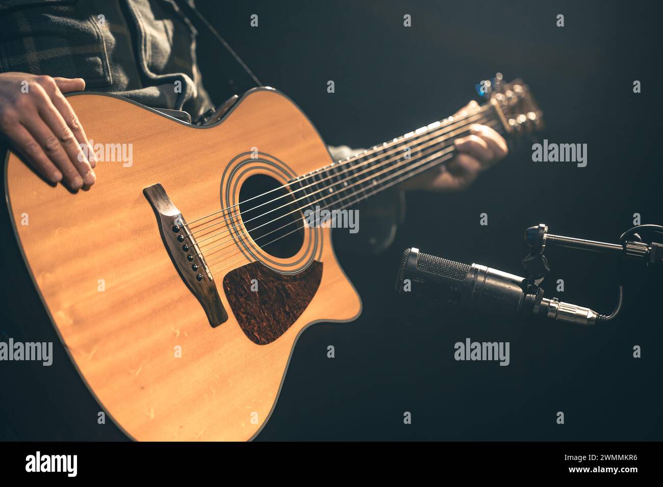 Male musician playing acoustic guitar behind microphone in recording ...