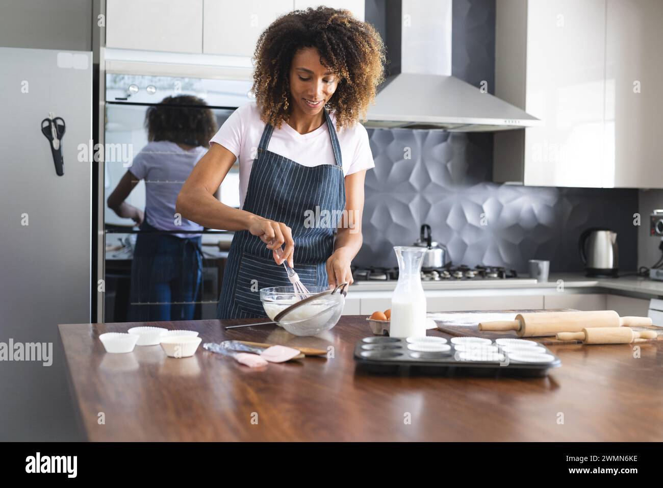 Biracial woman prepares dough in a modern kitchen. She's focused on ...