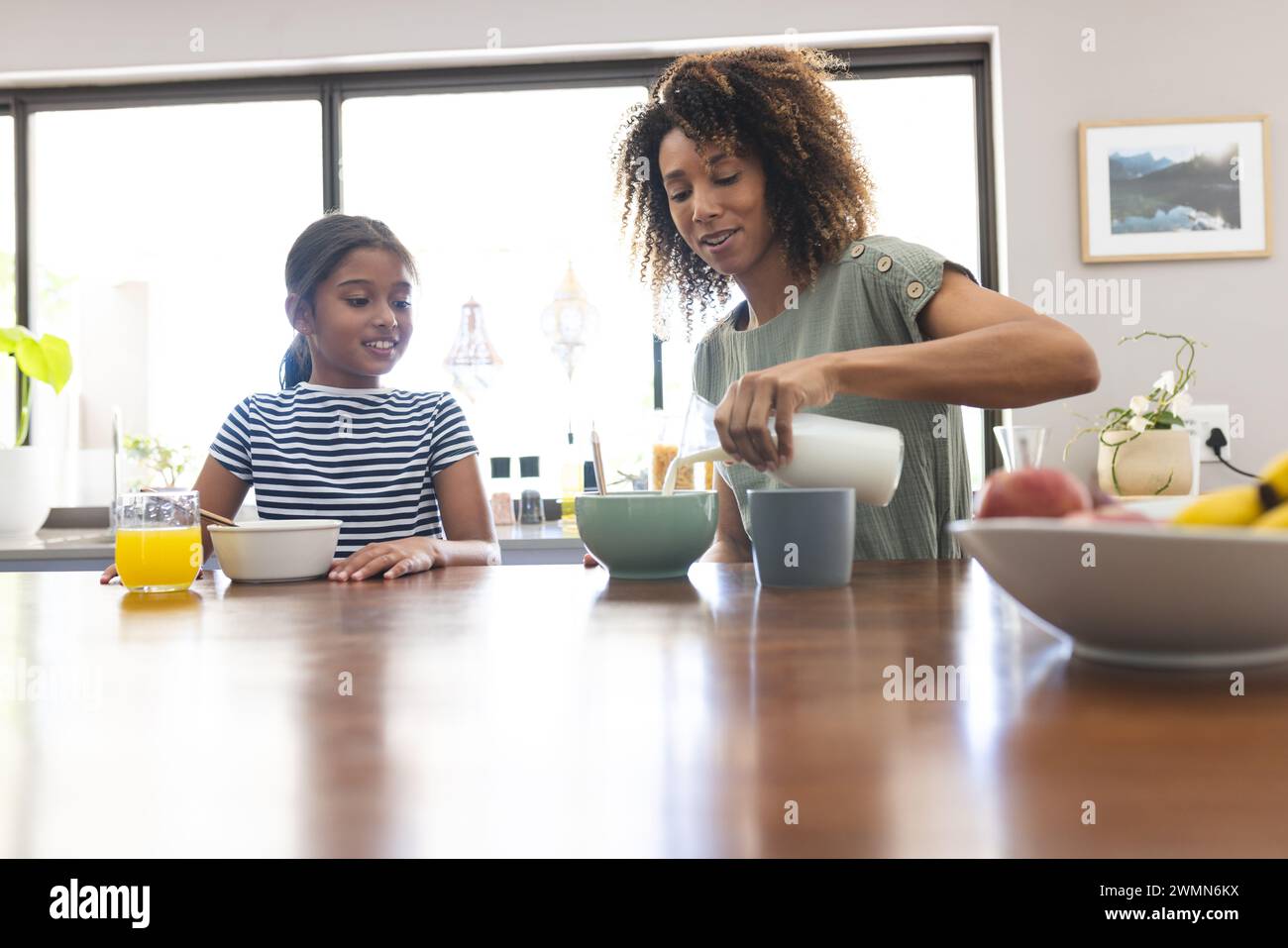 Biracial mother pours milk and cereal at home for her daughter, with ...